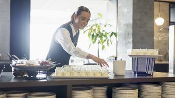 Disposição de buffet com pratos, bandeja e um atendente.