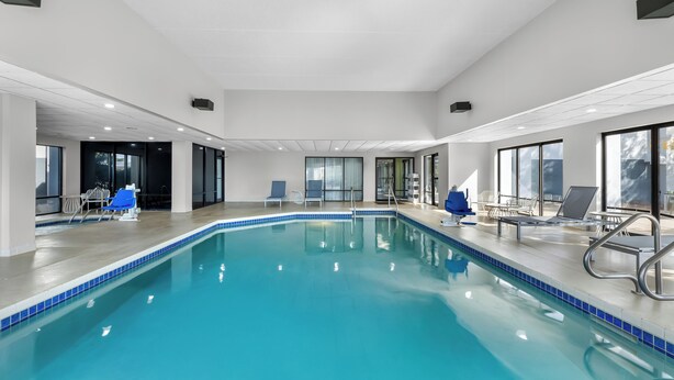 Piscina interna com água azul cristalina, rodeada por espreguiçadeiras e borda em azulejo.