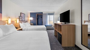 Quarto de hotel com duas camas, uma televisão, uma escrivaninha e um espelho.
