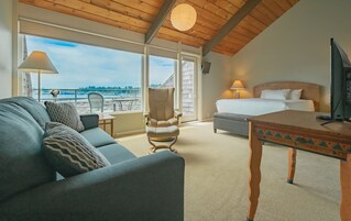 Quarto de hotel com varanda, cama, sofá, cadeira e mesa.
