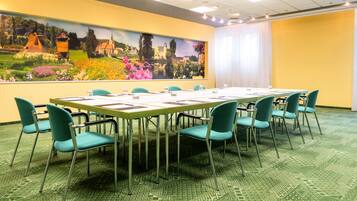 Uma sala de conferências com uma mesa comprida, cadeiras cor verde-água e um grande mural de uma paisagem na parede.