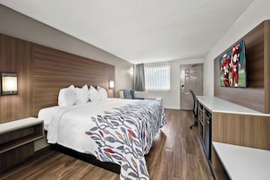 Quarto de hotel com uma cama grande, uma escrivaninha, televisão e banheiro visível através de uma porta aberta.
