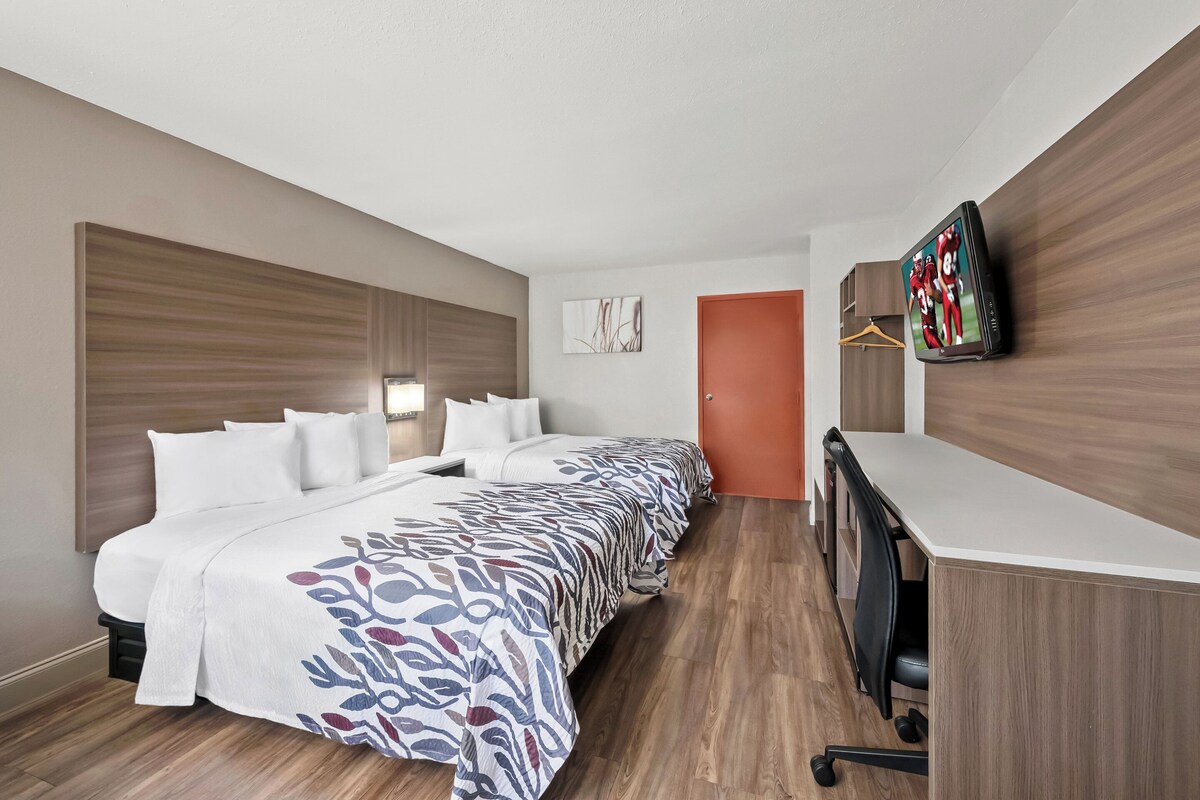 Quarto de hotel com uma cama grande, uma escrivaninha, uma televisão e uma porta.