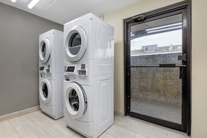 Uma lavanderia com duas máquinas de lavar roupa frontais empilhadas e uma porta de vidro que dá para o exterior.