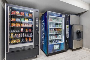 Duas máquinas de venda automática com lanches e bebidas, e uma geladeira.
