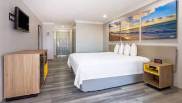 Quarto de hotel moderno com uma cama grande, uma TV fixada na parede e uma pintura de um pôr do sol sobre o oceano.