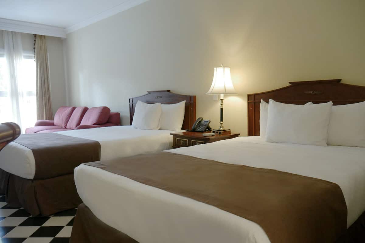 Quarto de hotel com duas camas, uma mesa com abajur, telefone e uma cadeira.