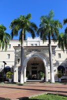 Entrada de hotel com arco ornamentado, palmeiras e céu azul límpido.