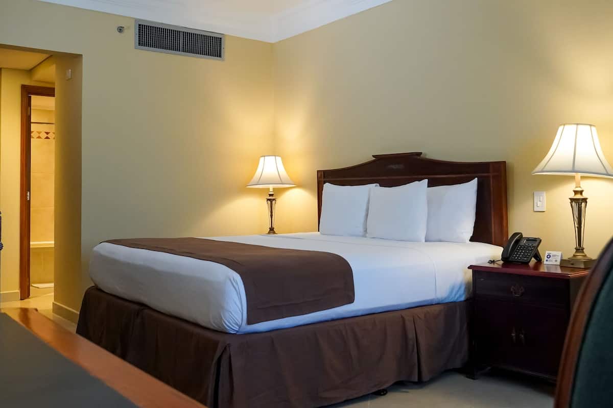 Quarto de hotel com uma cama grande, duas luminárias de cabeceira, um telefone e uma escrivaninha com abajur.
