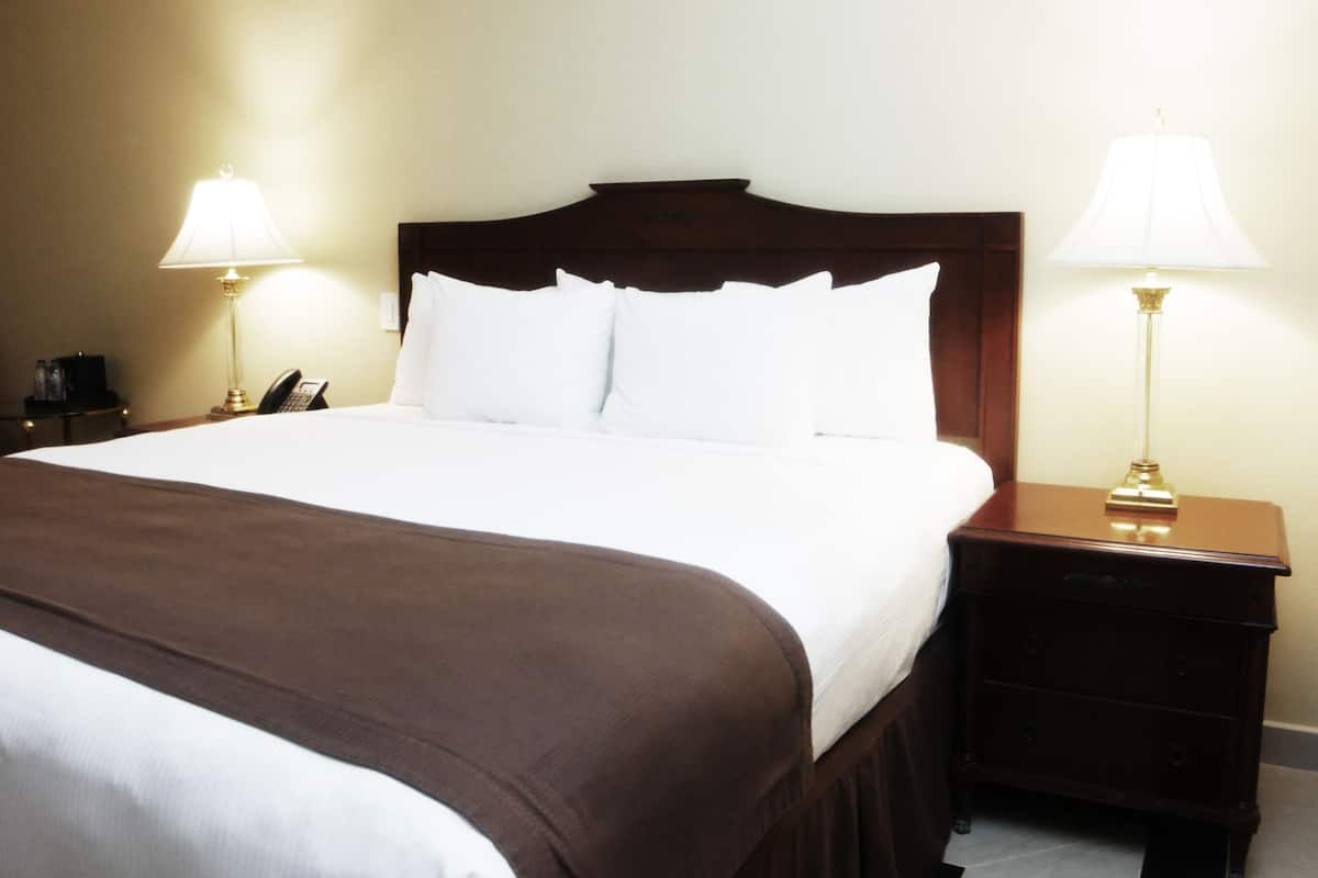 Quarto de hotel com uma cama grande, duas mesas de cabeceira com luminárias, um telefone e uma pequena mesa com cafeteira.