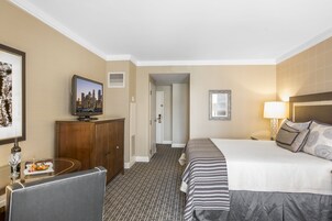 Quarto de hotel com cama, televisão, escrivaninha e cadeira, e uma mesa de jantar com um prato de comida.