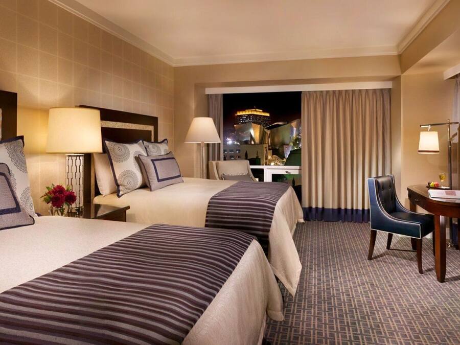Quarto de hotel com duas camas, uma escrivaninha, uma cadeira e uma televisão.
