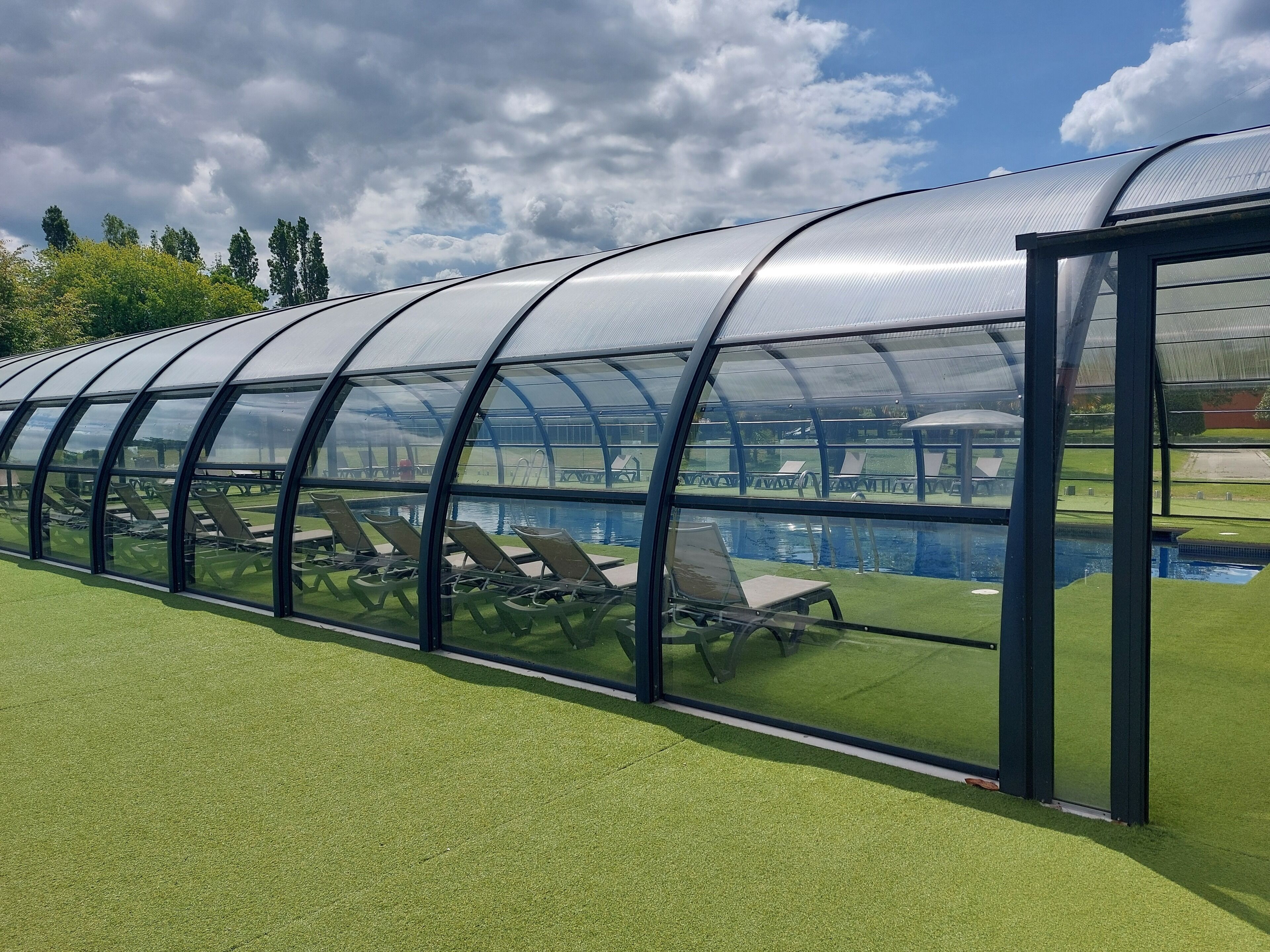 Área de piscina coberta com espreguiçadeiras e vista para a piscina.