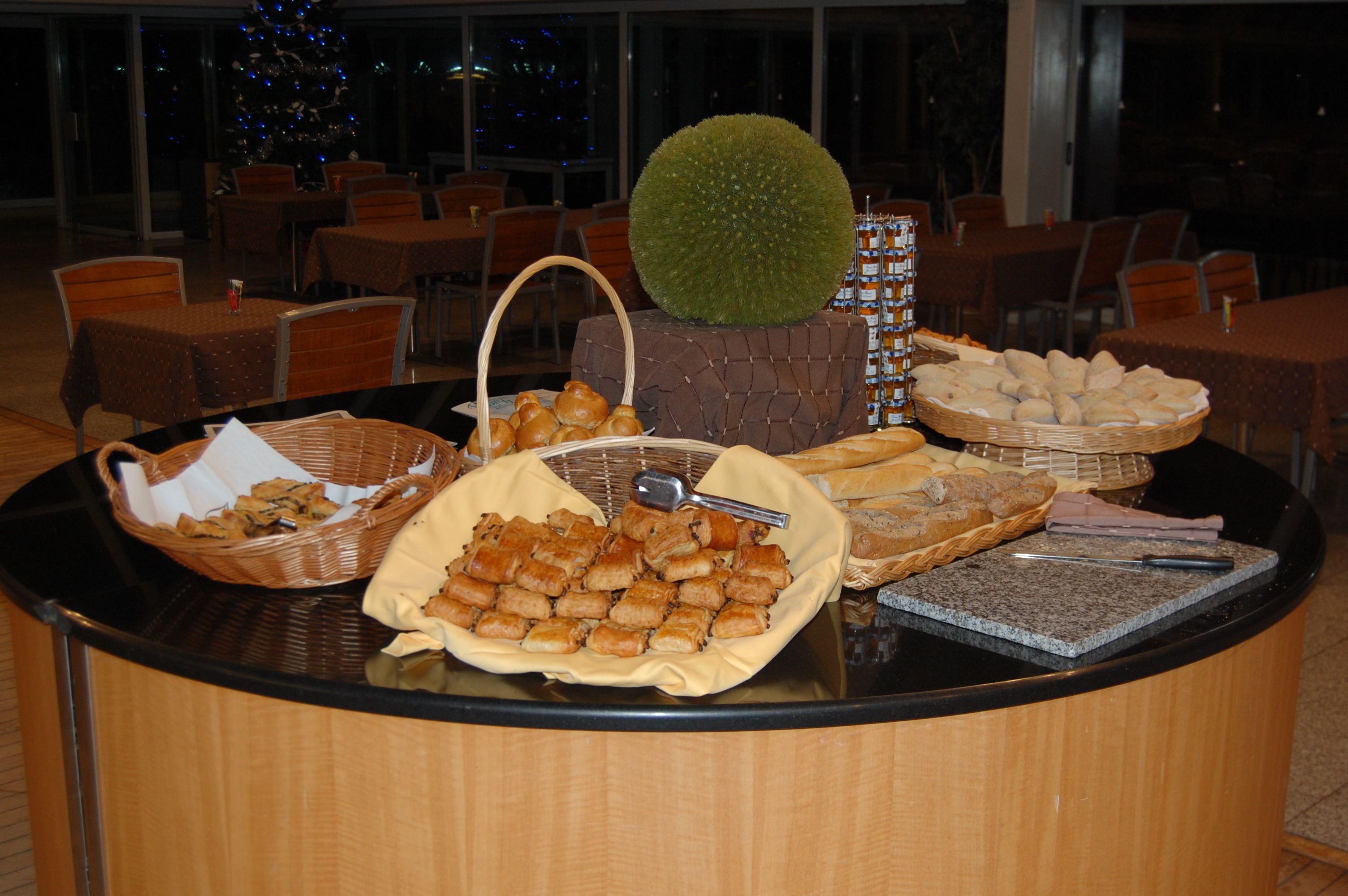 Buffet com diversos produtos de panificação e uma árvore de Natal ao fundo.