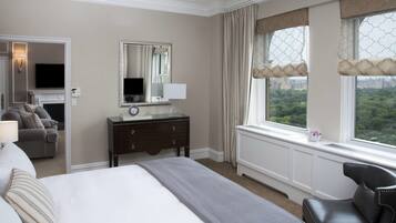 Quarto de hotel com uma cama grande, cômoda, cadeira, televisão e janela com vista para árvores.