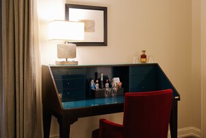 Uma mesa com luminária, uma cadeira e uma seleção de garrafas.
