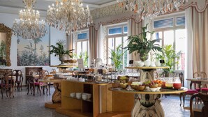 Uma sala de jantar bem iluminada com várias luminárias pendentes, um buffet central com diversos pratos e algumas plantas em vasos.