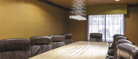 Uma sala de conferências com uma mesa comprida e cadeiras de couro, um lustre e uma janela com cortinas.