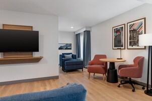 Quarto de hotel moderno com televisão de tela plana, sofá, duas poltronas, uma mesa pequena e obras de arte nas paredes.