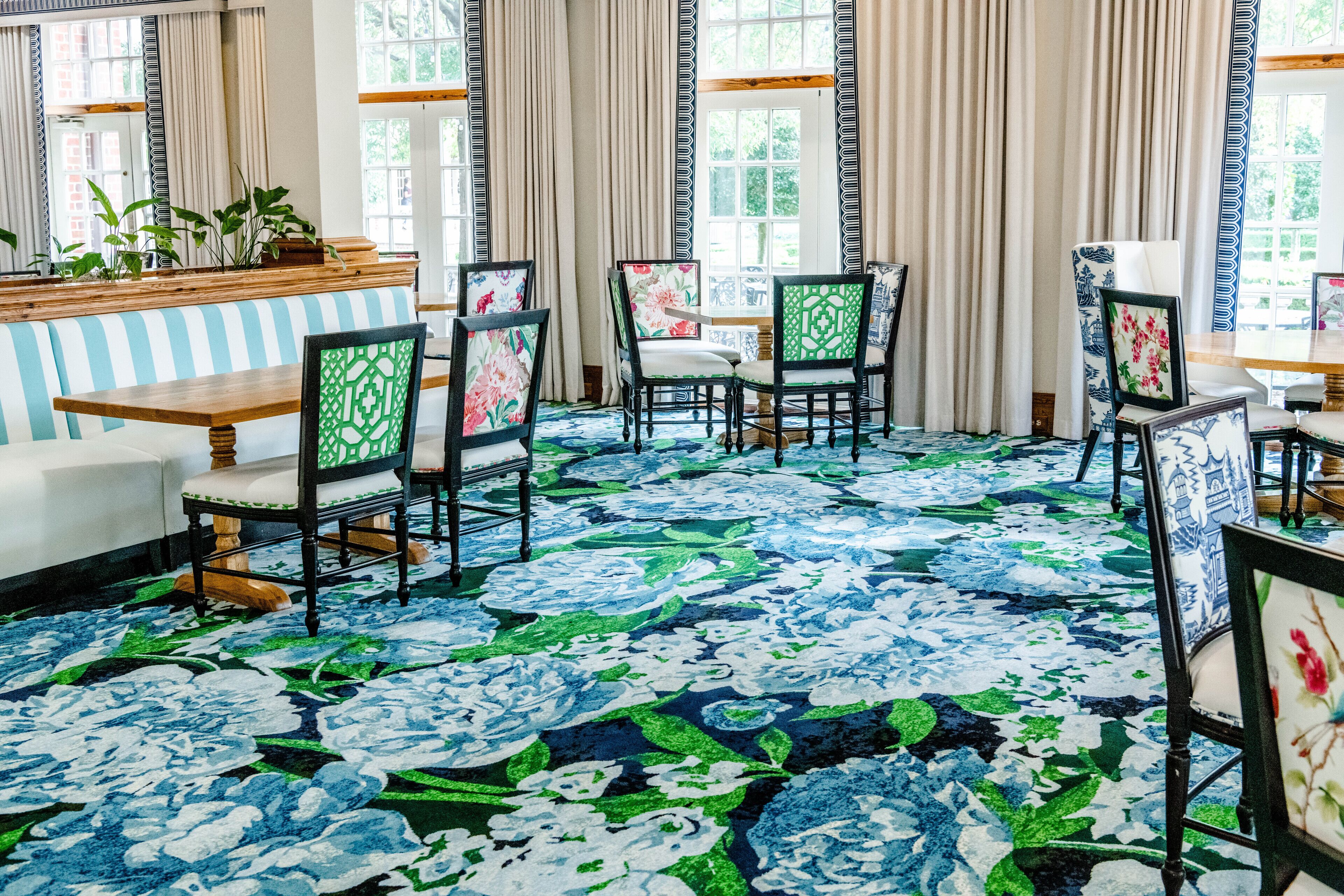 Um quarto com carpete floral, um banco riscado e cadeiras estampadas.