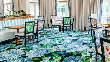 Um quarto com carpete floral, um banco riscado e cadeiras estampadas.