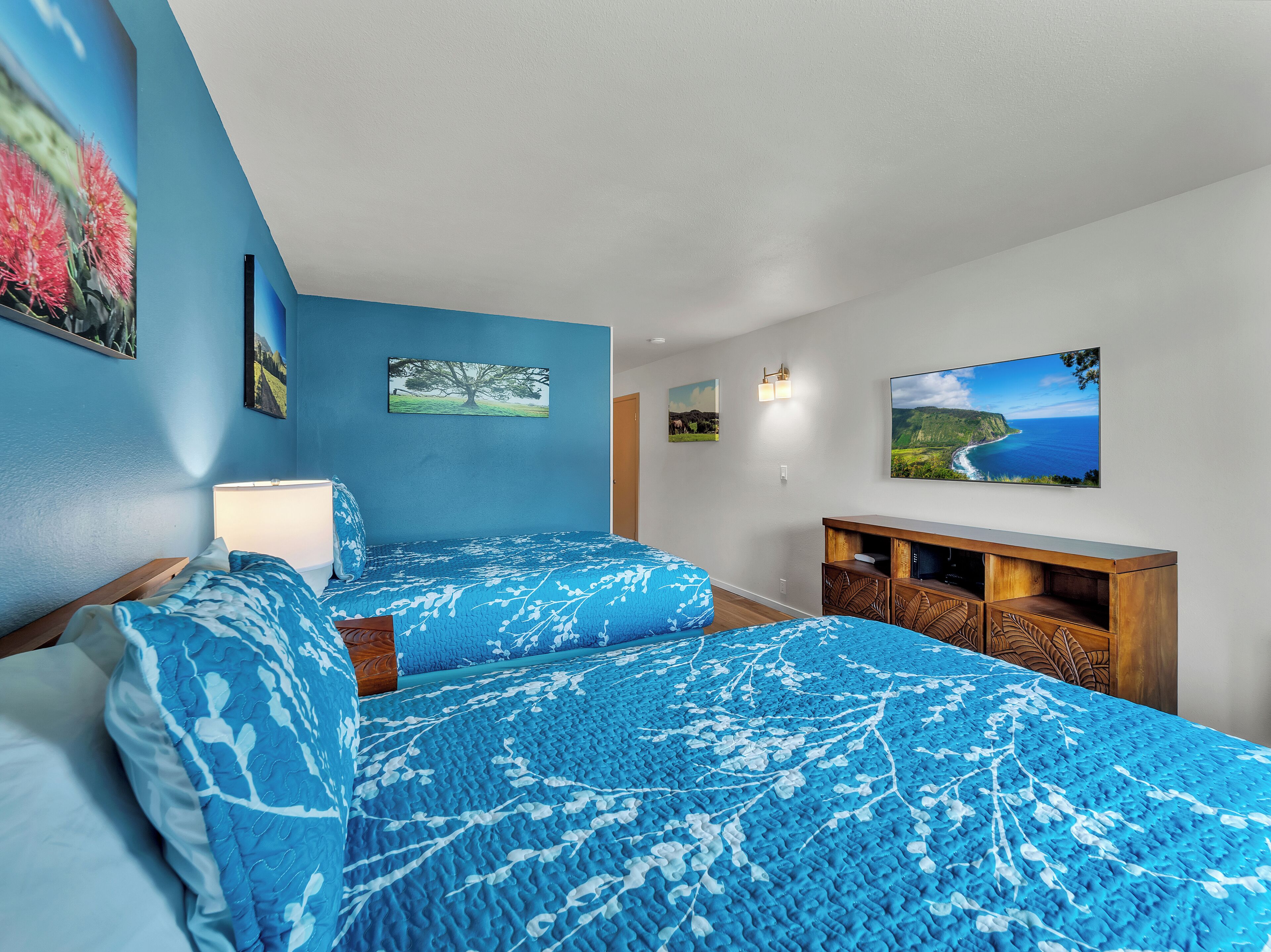 Quarto com duas camas, cômoda de madeira e obras de arte penduradas na parede.