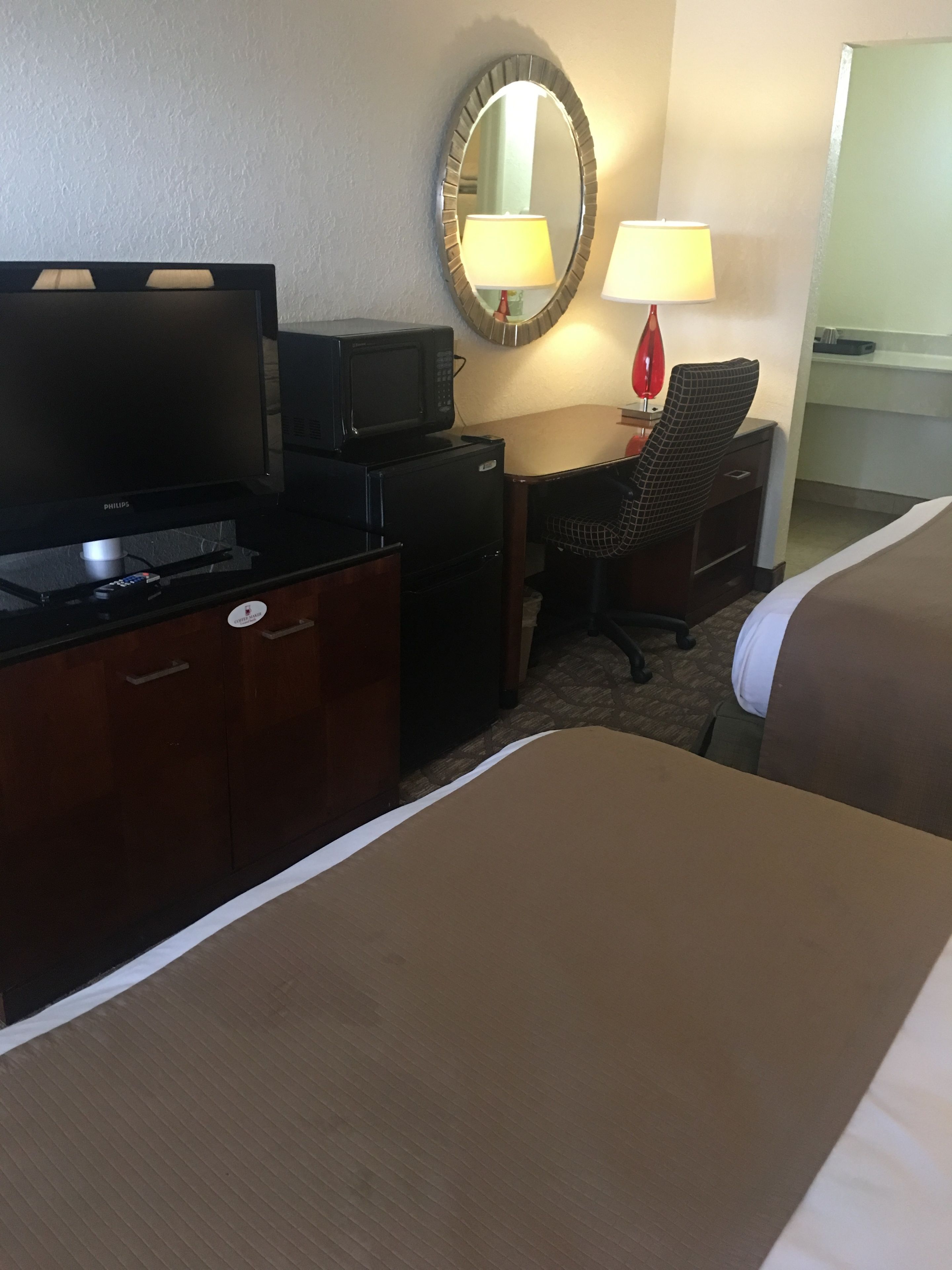 Quarto de hotel com cama, escrivaninha com abajur, televisão e micro-ondas.