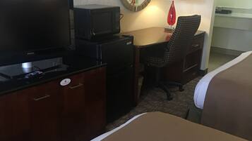 Quarto de hotel com cama, escrivaninha com abajur, televisão e micro-ondas.