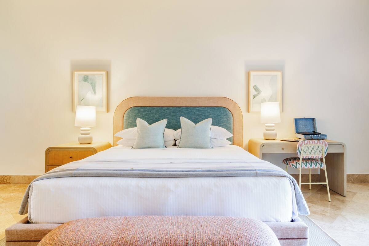 Quarto de hotel bem arrumado, com cama, mesas de cabeceira, escrivaninha e uma cadeira.