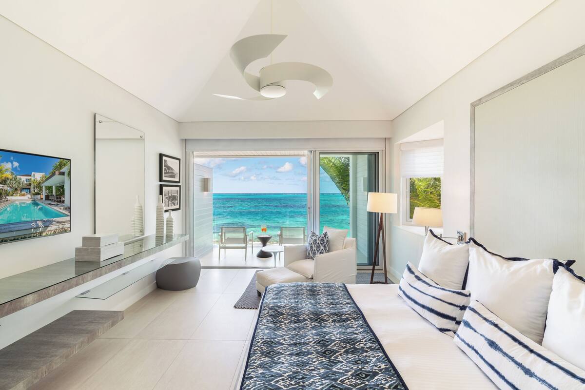 Quarto de hotel moderno com uma cama grande, uma mesa de centro de vidro, um sofá e vista para o oceano.