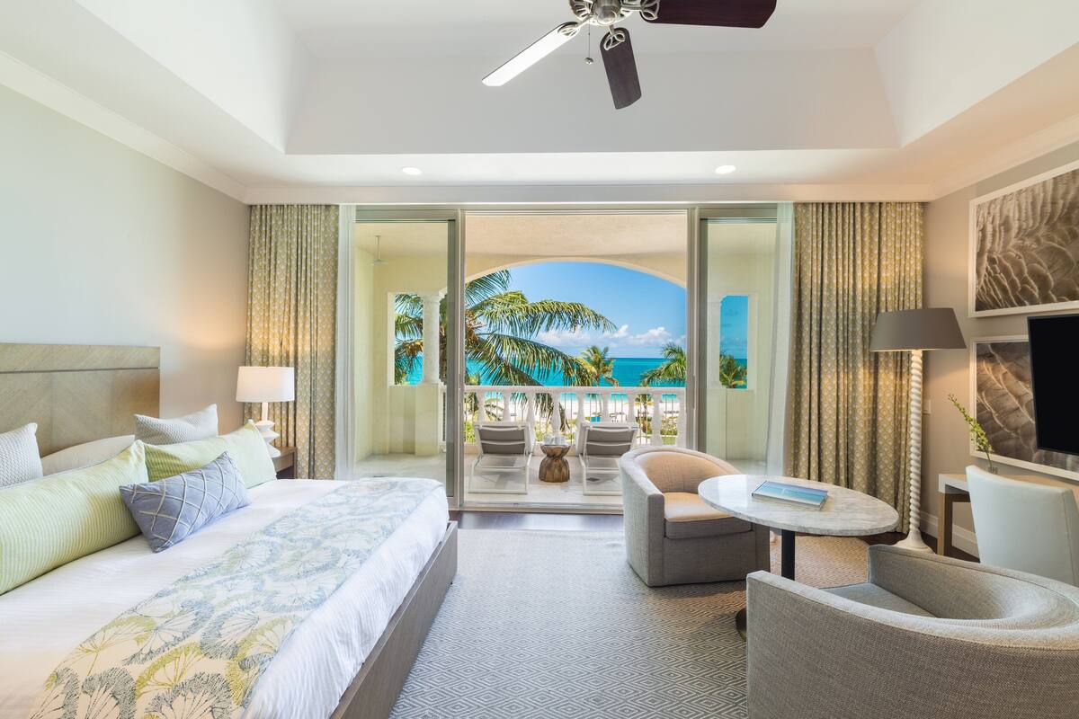 Quarto de hotel com cama, área de estar com mesa e varanda com vista para o oceano.