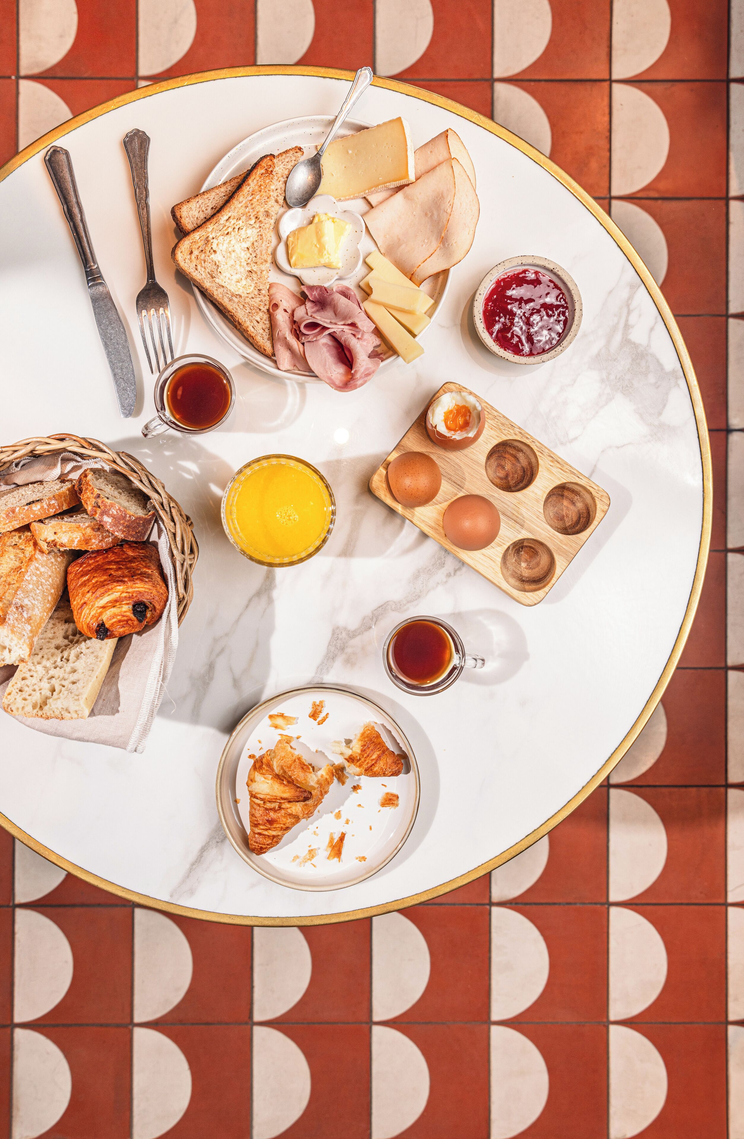 Uma mesa de mármore com torradas, ovos, fiambre, queijo e pastelaria para o pequeno-almoço.