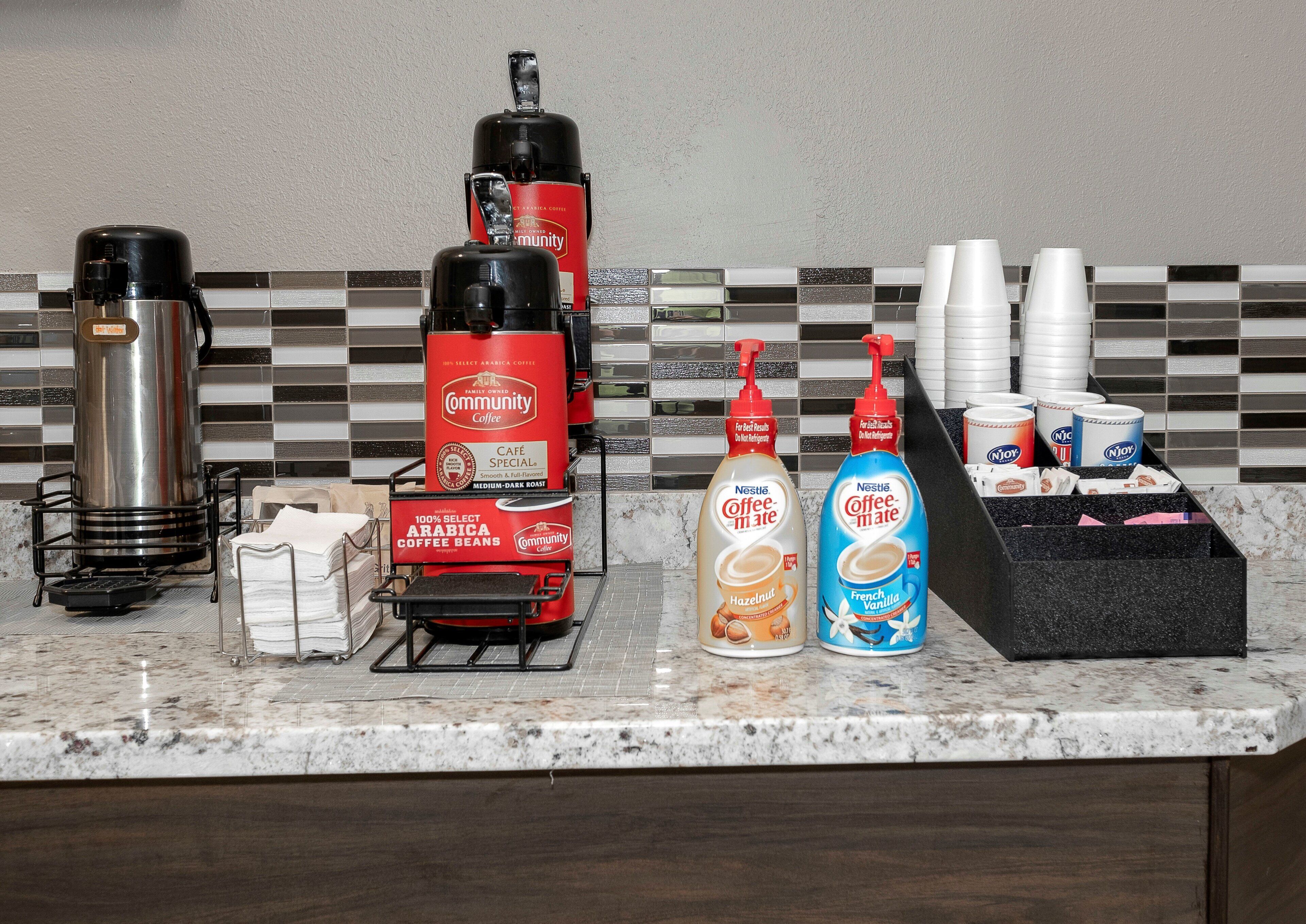 Uma bancada de cozinha com máquinas de café, cápsulas de café e copos descartáveis.
