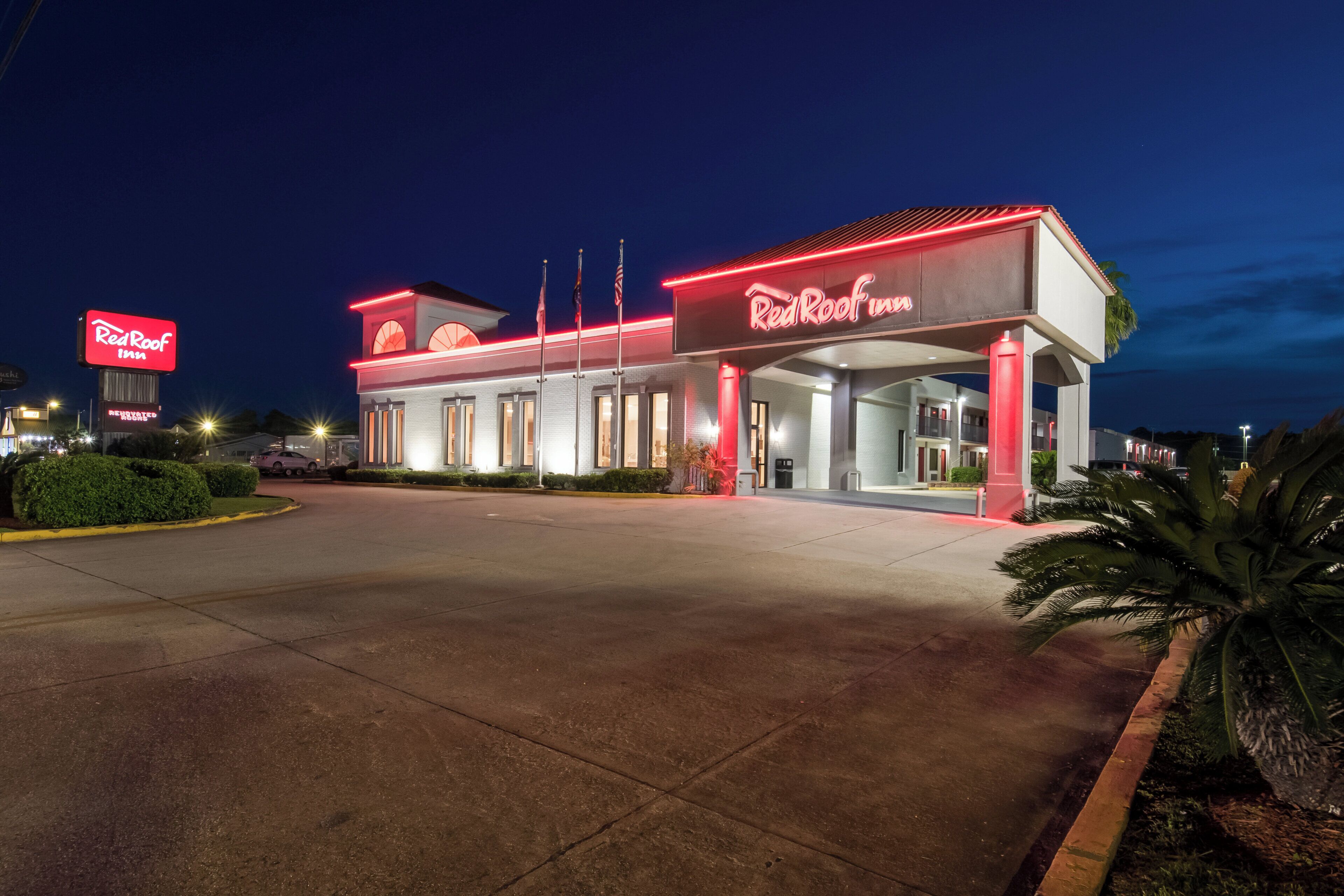 Um Red Roof Inn com uma grande placa, estacionamento e entrada bem iluminada.