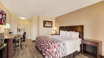 Quarto de hotel com cama, mesa de cabeceira, luminária, escrivaninha com cadeira e televisão.