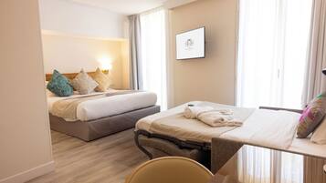 Quarto de hotel com duas camas, uma escrivaninha, uma cadeira, televisão na parede e janela com cortinas.