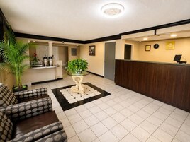 Um saguão de hotel com balcão de recepção, máquina de café, planta em vaso, sofá e chão de azulejos.