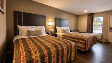 Quarto de hotel com duas camas, uma mesa de cabeceira, uma luminária e uma janela com cortinas.