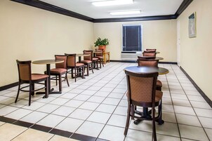 Sala de conferências com várias mesas e cadeiras, um vaso de planta e uma janela com persianas.