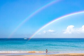 Uma praia com um veleiro e um arco-íris.