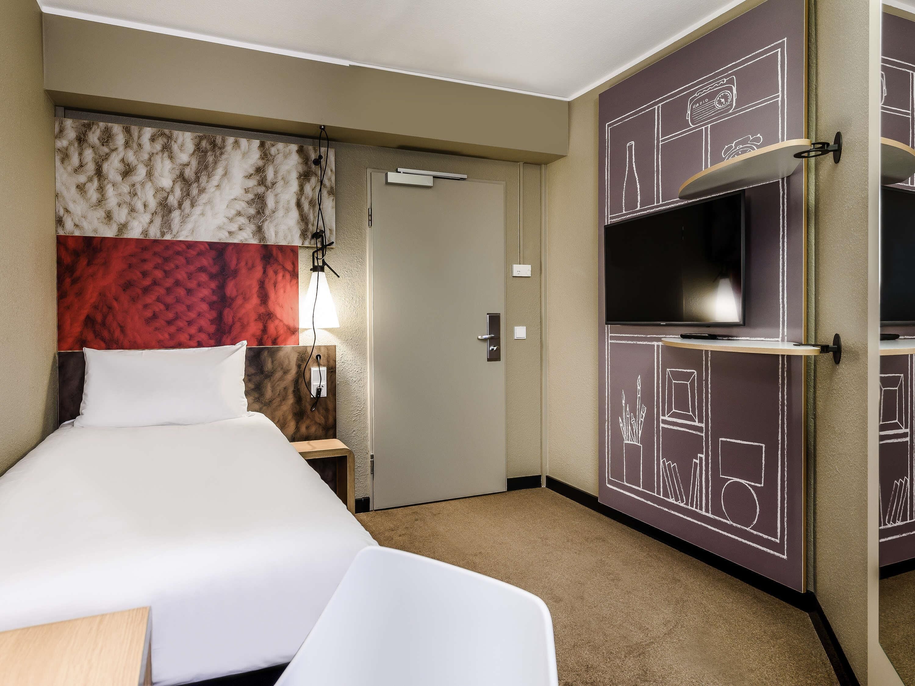 Quarto de hotel com cama, escrivaninha, televisão e armário com desenhos de quadro negro.