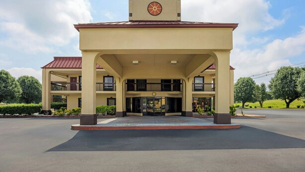Um edifício de dois andares com uma entrada central, um relógio no telhado e uma área ajardinada em frente.
