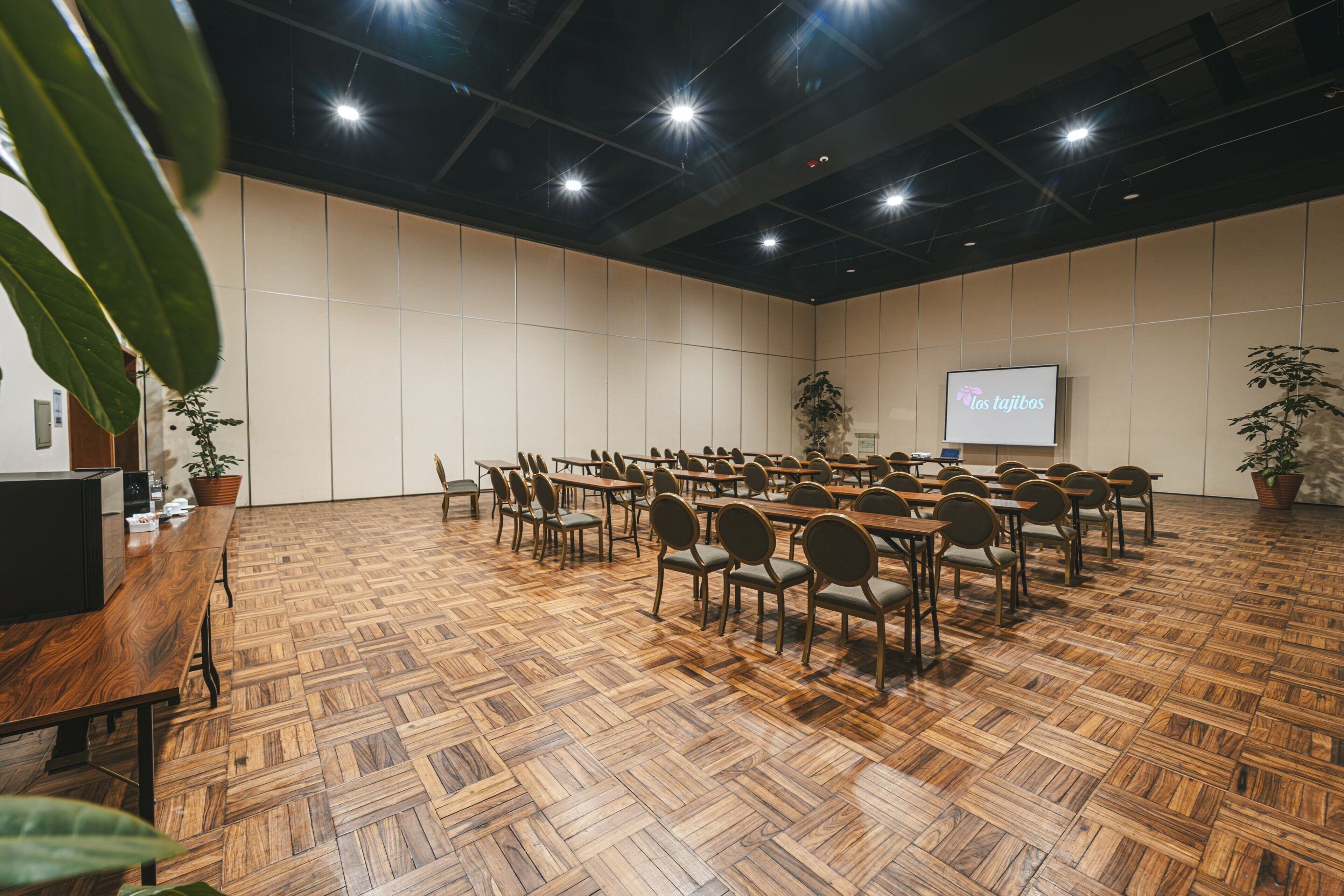 Uma sala de conferências com piso de tacos de madeira, várias mesas e cadeiras dispostas para uma reunião.