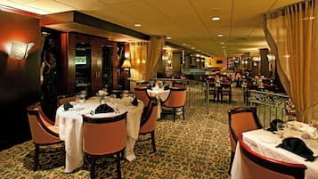 Um espaço de refeições de hotel com mesas preparadas para o jantar, cadeiras e um tapete estampado.
