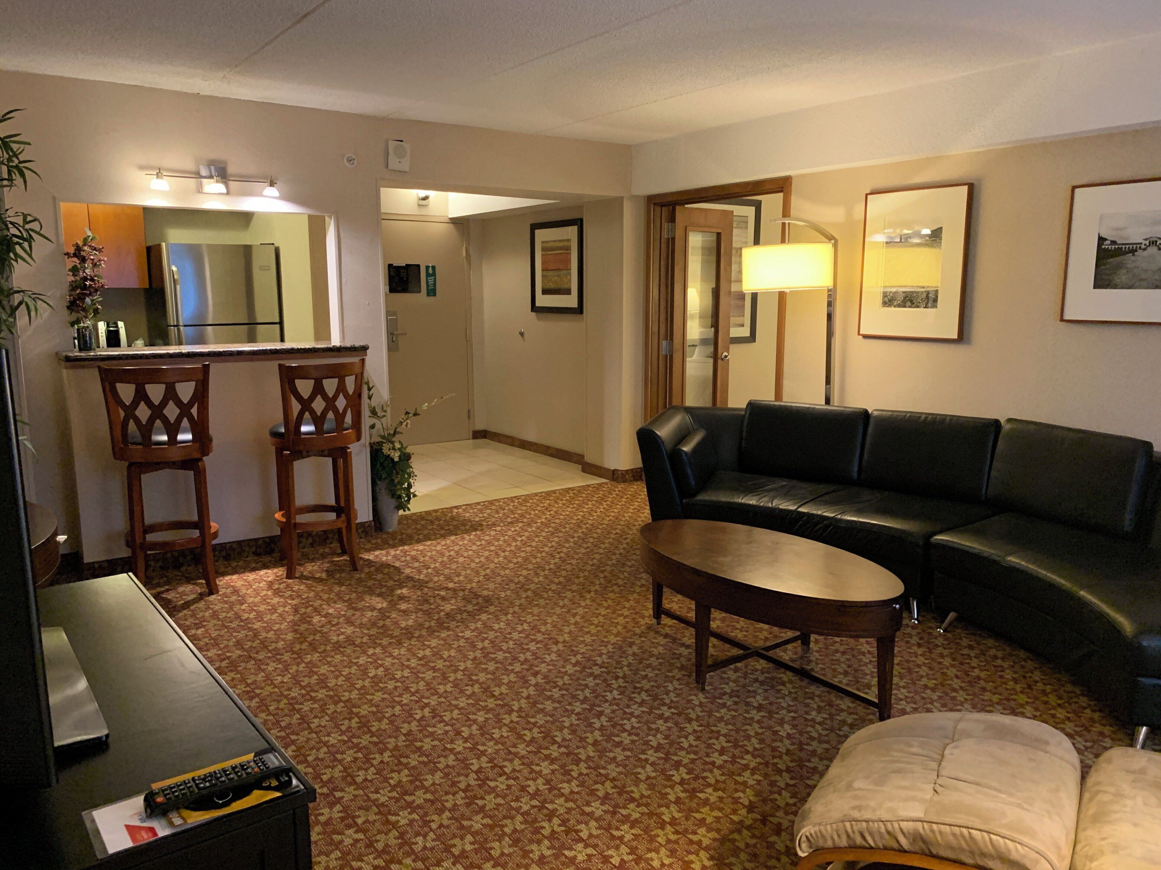 Quarto de hotel com sala de estar, bar, sofá, mesa de centro e televisão.