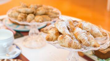 Uma mesa com diversos doces e pastelaria à mostra, incluindo croissants e outros produtos de panificação.