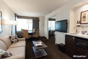 Quarto de hotel com sofá, mesa de centro, televisão, área de refeições com cadeiras e cozinha equipada com pia e micro-ondas.