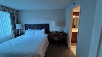 Quarto de hotel com uma cama grande, uma escrivaninha com cadeira e uma porta para o banheiro.