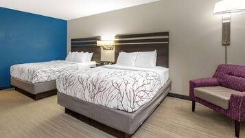 Quarto de hotel com duas camas, uma mesa de cabeceira, um abajur e uma poltrona roxa.