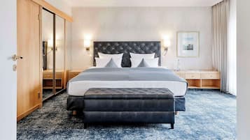 Quarto de hotel com uma cama grande, um guarda-roupa de madeira, uma escrivaninha e uma janela com cortinas.